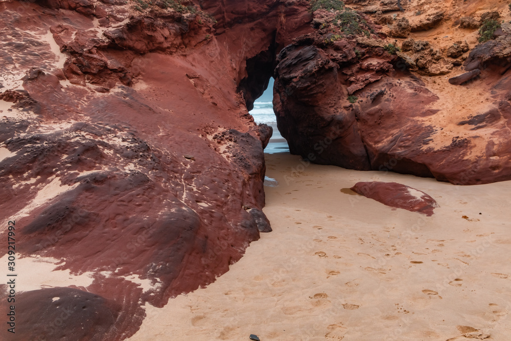 Red ocean rocks at the beach in cloudy weather light. Praia da Bordeira ...