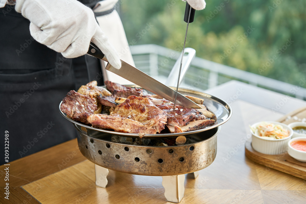 The waiter is butchering with a knife. Various grilled meat set ...