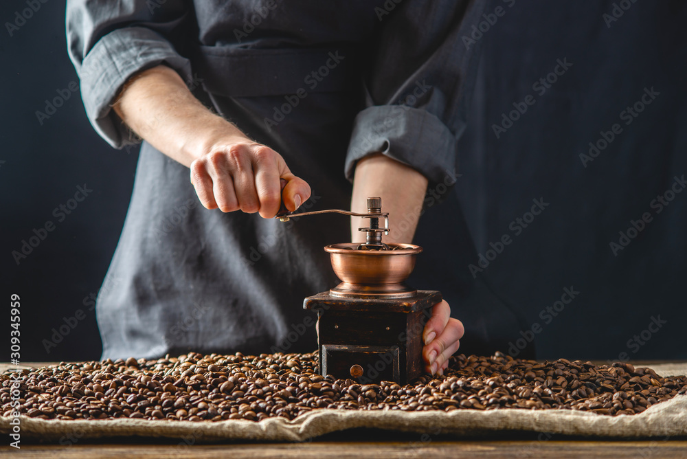 Hands baristas in a dark apron grind on a manual grinder fragrant ...