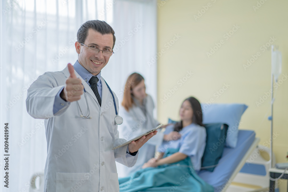 A professional doctor standing in a room with a patient lying in bed ...