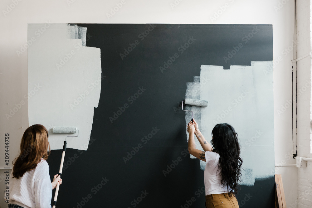 two women painting a backdrop in a modern bright industrial studio ...