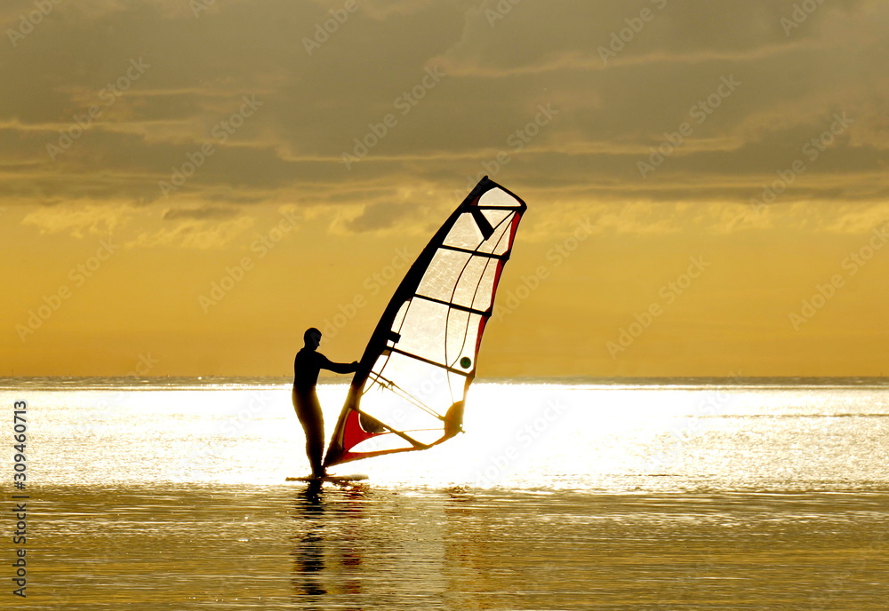 Windsurfing in the rays of the setting sun. Silhouette of a man on a ...