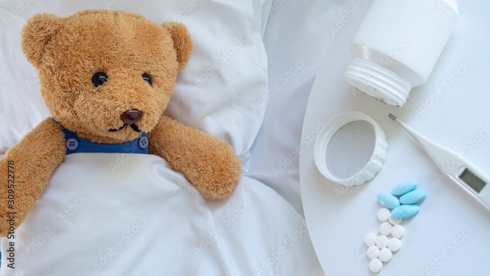 The sad teddy bear had a headache and fever, lying ill in the bed ...