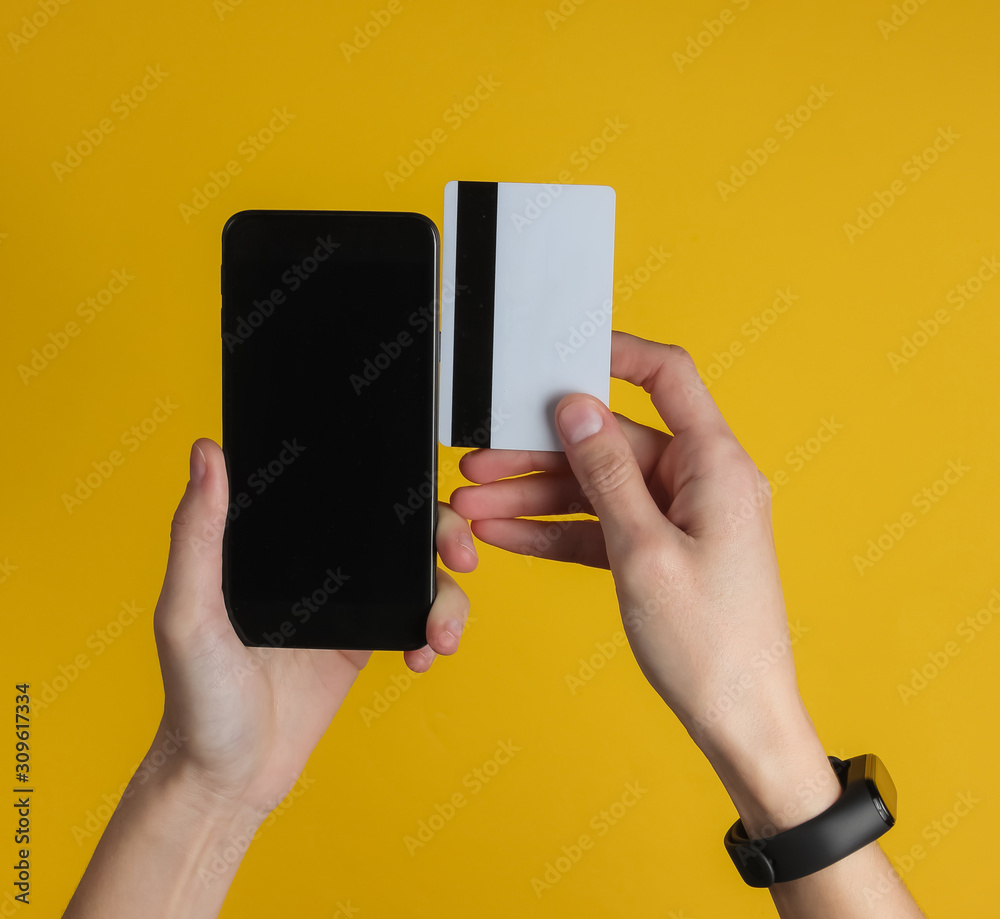 Hand with smart bracelet holding bank card and smartphone on yellow ...