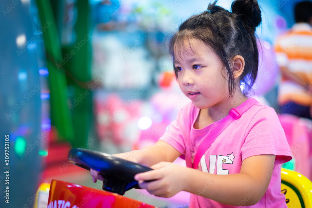 Little asian girl playing Racing car arcade game machine in Game center ...