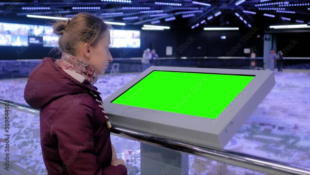 Woman looking at blank digital interactive green display kiosk at ...