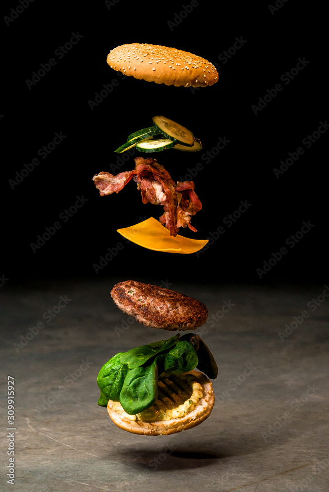 Flying cheeseburger ingredients on dark background of concrete ...