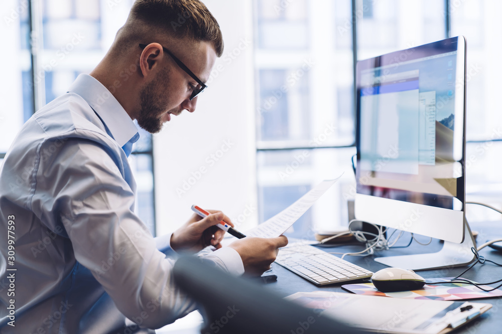 Serious manager checking document with pen at working table Stock Photo ...
