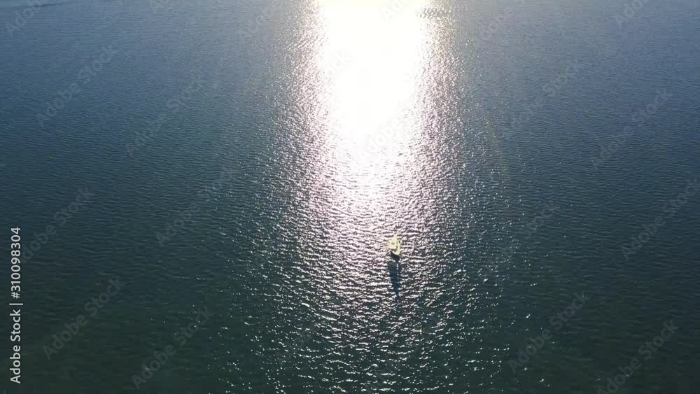 drone hovering above the blue water where a sailing boat crosses the ...