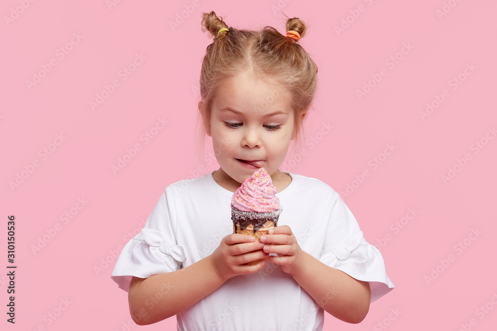 Cute child girl with pleasure eats tasty ice-cream on a pink studio ...
