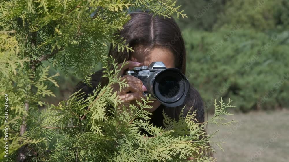 Paparazzi in the bush. A cute girl with a camera is hiding in the ...