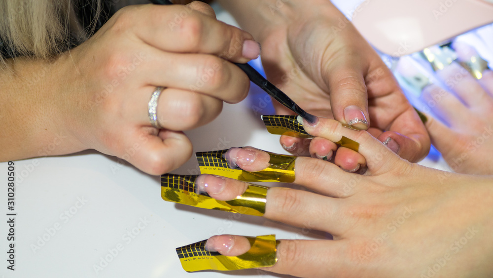 The master of the nail polish puts a fixative on the finger before ...