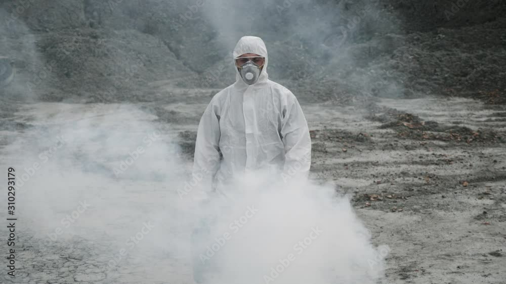 Lab technician in a mask and chemical protective suit, walks on dry ...