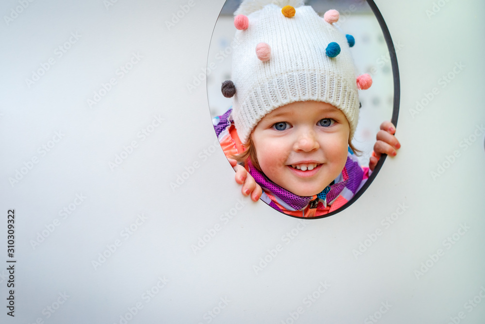 Child looks through a round hole on white playground. Smiles at the ...