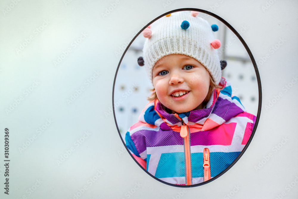 Child looks through a round hole on white playground. Smiles at the ...