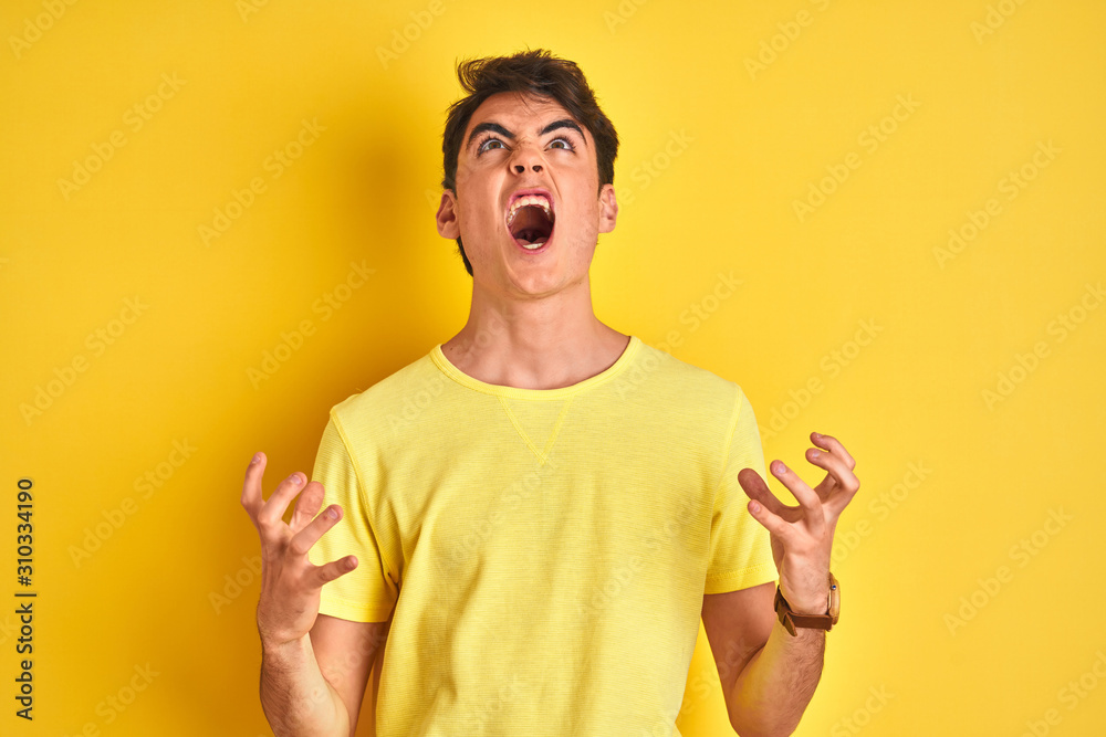 Teenager boy wearing yellow t-shirt over isolated background crazy and ...