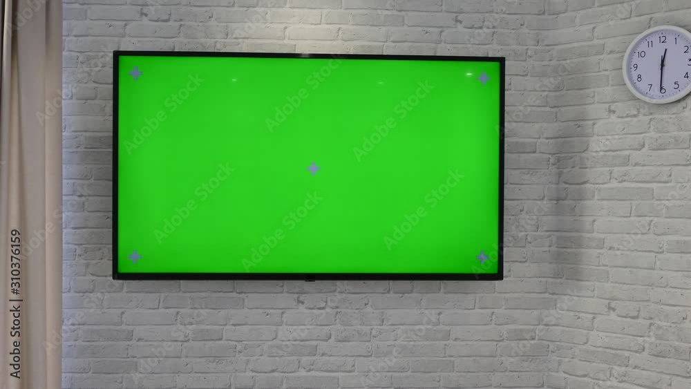 A green screen TV is hanging on the wall in the living room. Against the background of a brick ...