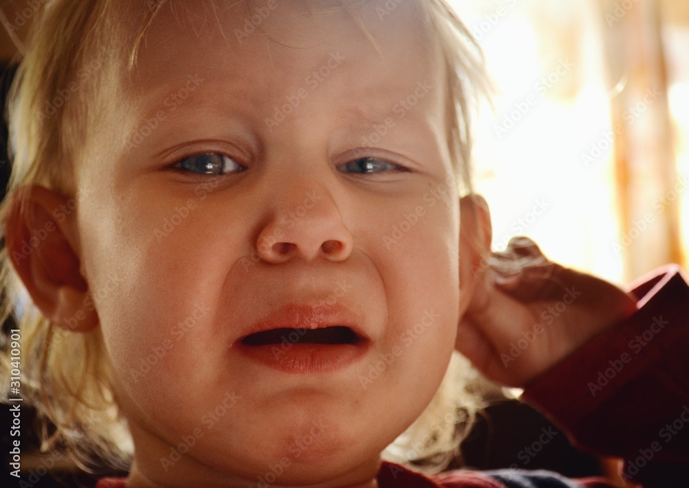 Portrait of a crying girl. The baby is crying. The child holds her ear ...