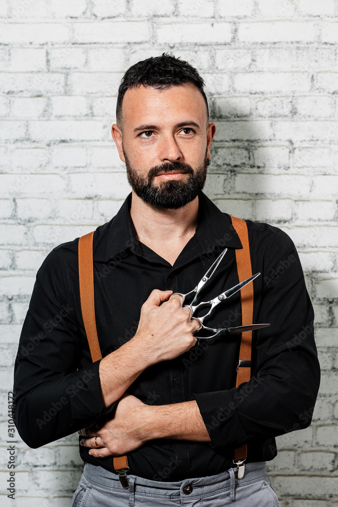 barbero caucásico con barba lleva unas tijeras en las manos y juega con ...