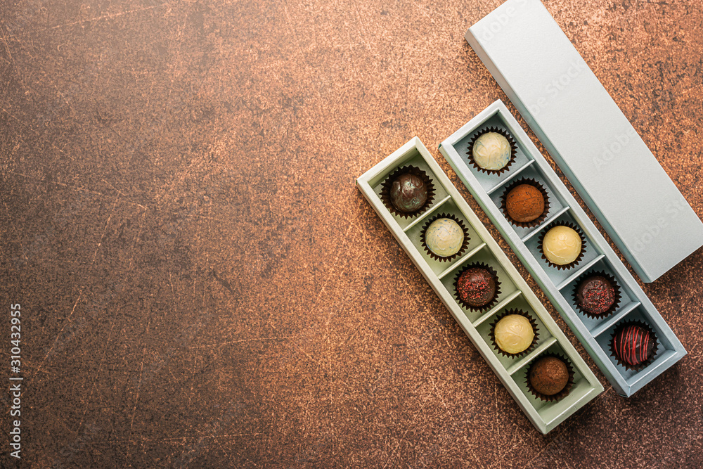 Handmade chocolates in different boxes on a dark background. Flat top ...