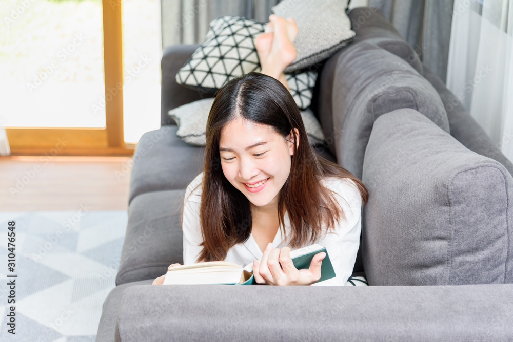 Relaxed young girl lying on cozy couch at home enjoying reading a book ...