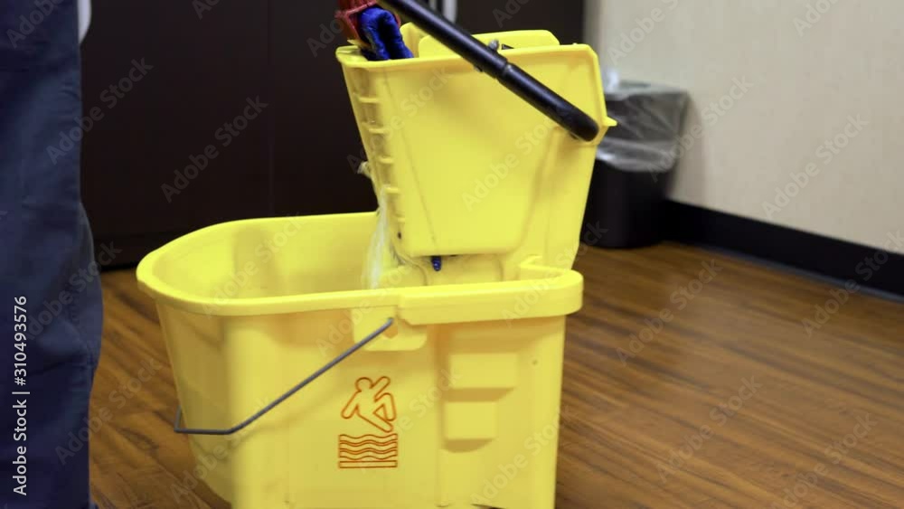 Woman janitor using a mop bucket and mop to clean the floor of hospital ...