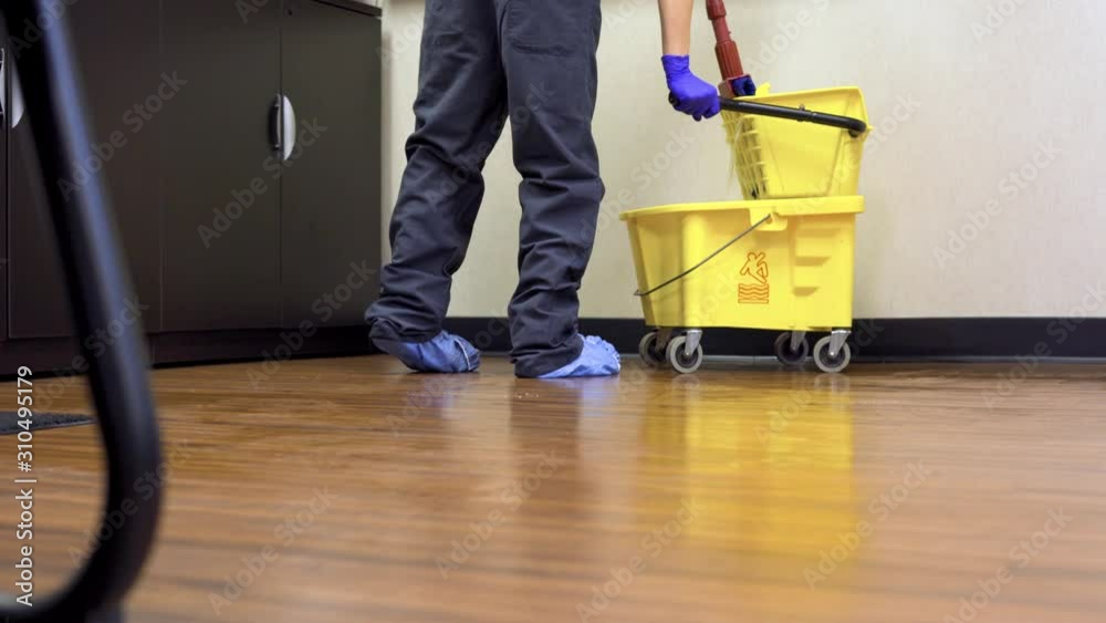 Woman janitor using a mop bucket and mop to clean the floor of hospital ...