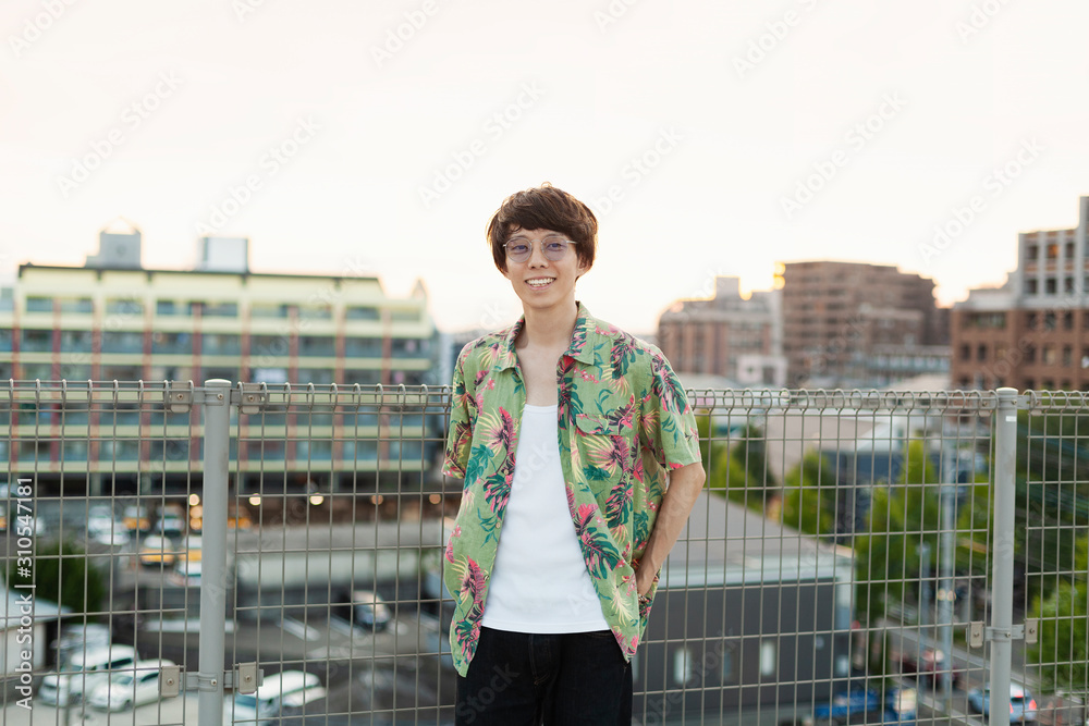 Young Japanese man standing on a rooftop in an urban setting, looking ...