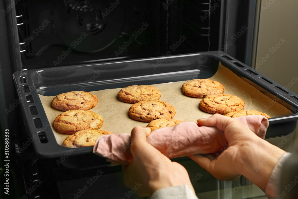 Woman taking baking tray with cookies out of oven Stock Photo | Adobe Stock