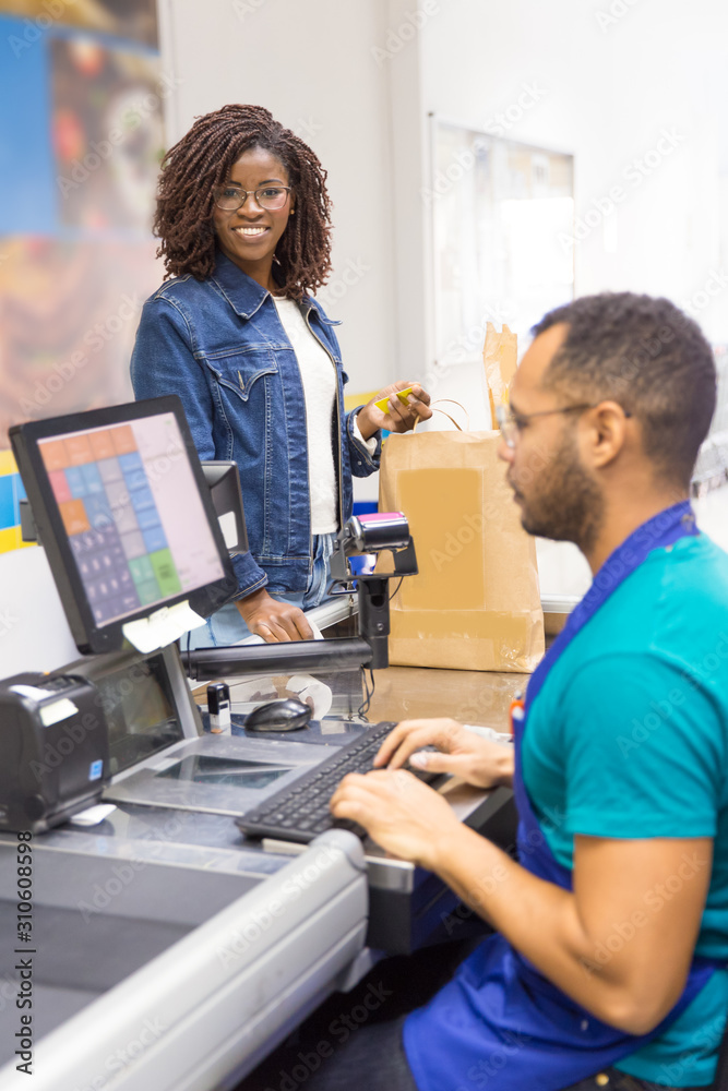 Smiling woman standing with credit card and packed food. Male cashier ...