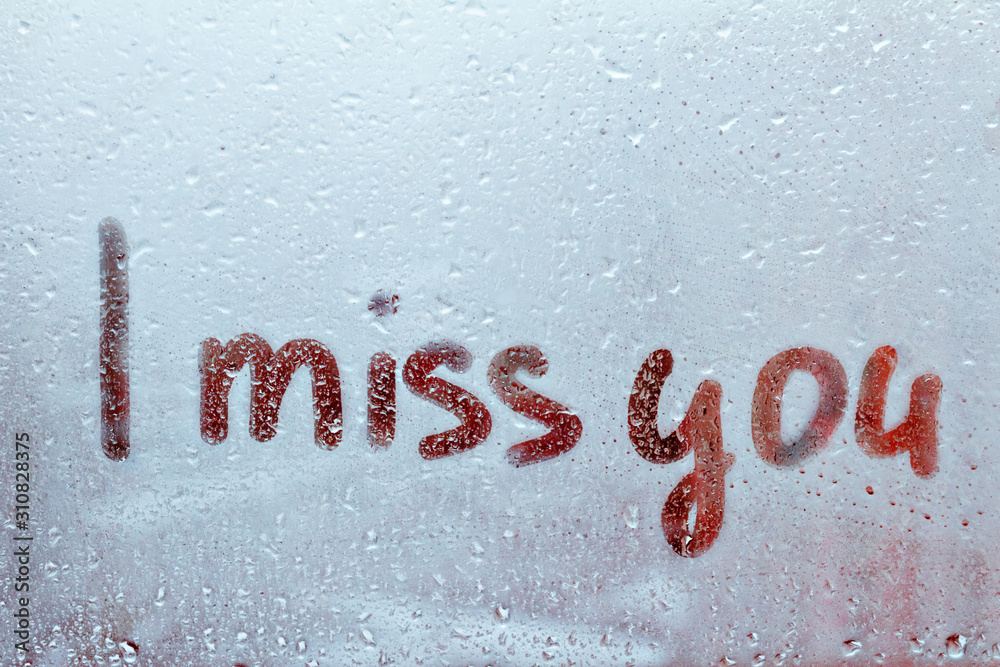 Foggy glass on window with written finger word red color I miss you ...
