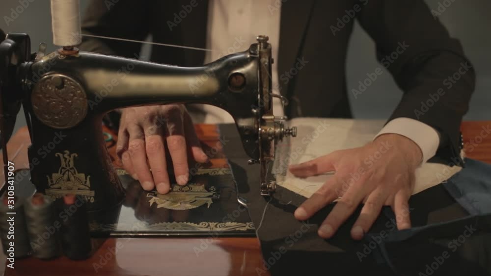 Slow motion footage of a tailor sewing two cloths together on his ...