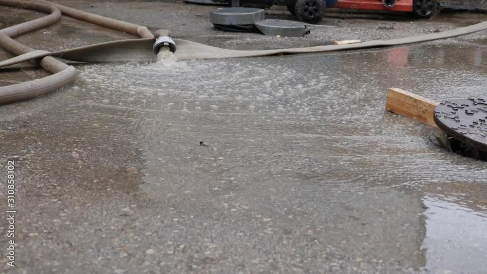 Close up footage of a water hose at a flooded area, people are pumping ...