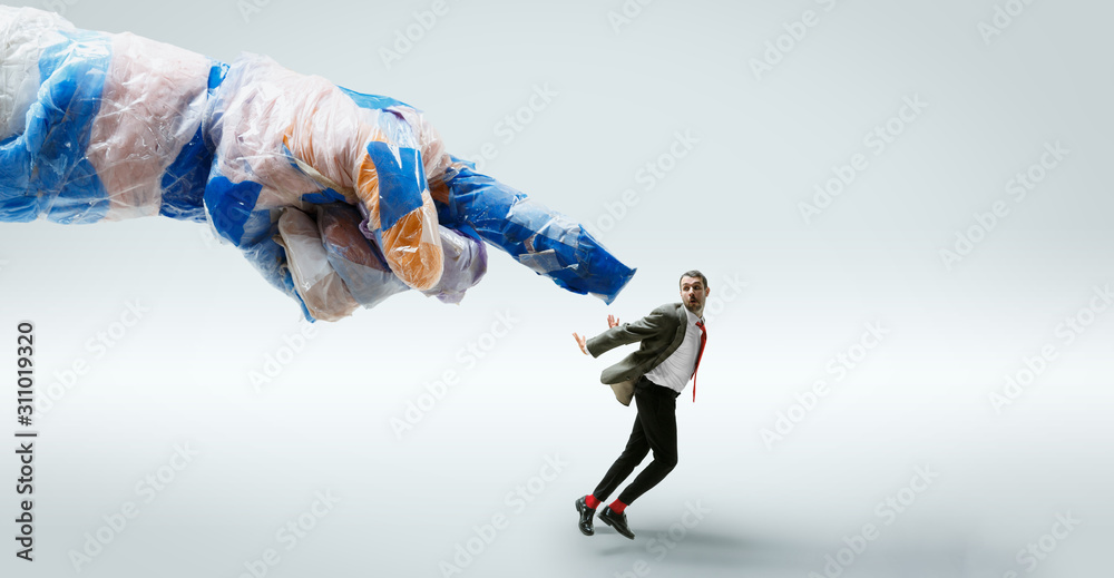Young caucasian man avoiding big plastic hand on white studio ...