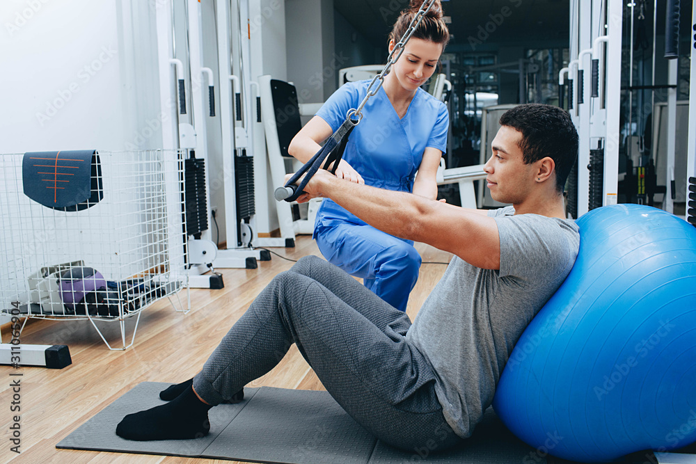 kinesiologist helps a mixed race man doing exercises to strengthen his ...