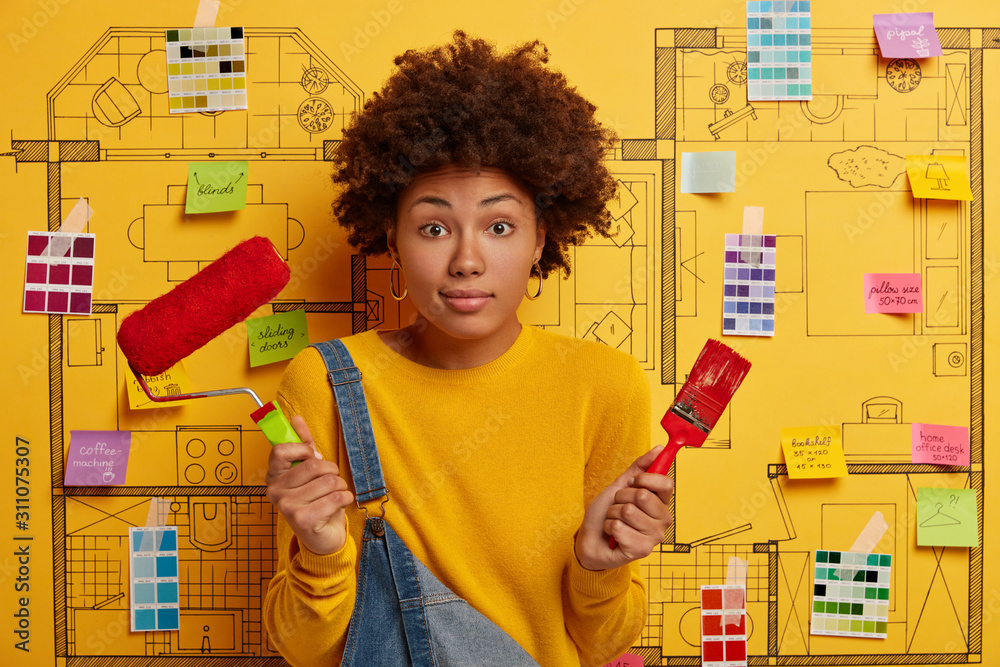 Headshot of curly dark skinned woman painter looks confusingly at ...