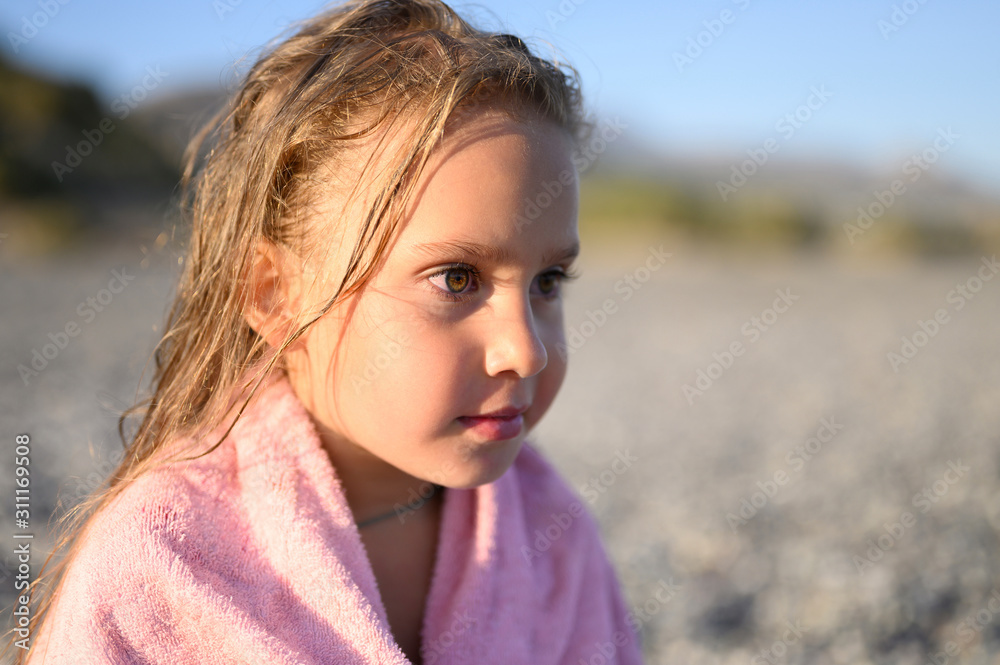 dreamy six year old little girl resting on the sea beach after swimming ...
