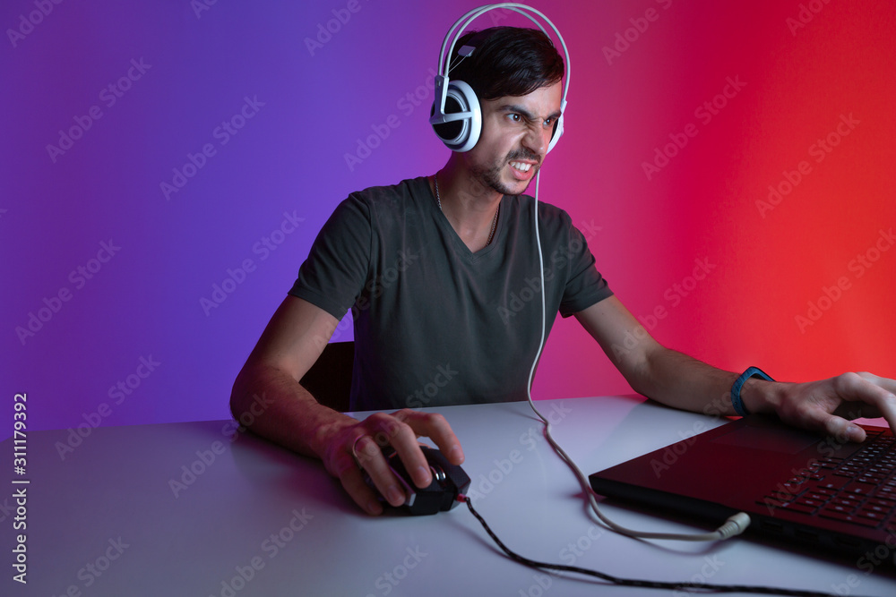 Portrait of an angry gamer playing video games on computer in dark room ...