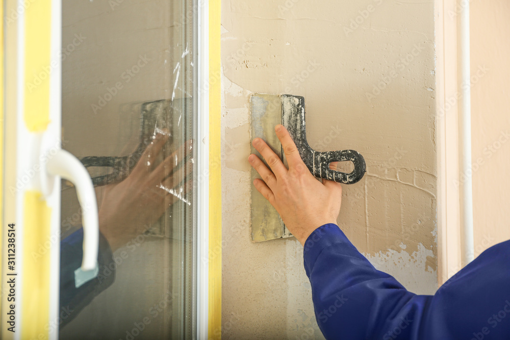 Professional worker plastering window area with putty knife indoors ...