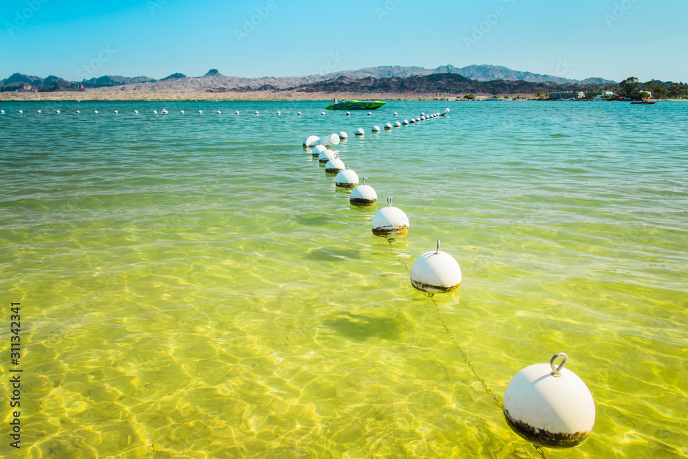 Line of white buoys and fast boat silhouette in quiet turquoise blue to ...