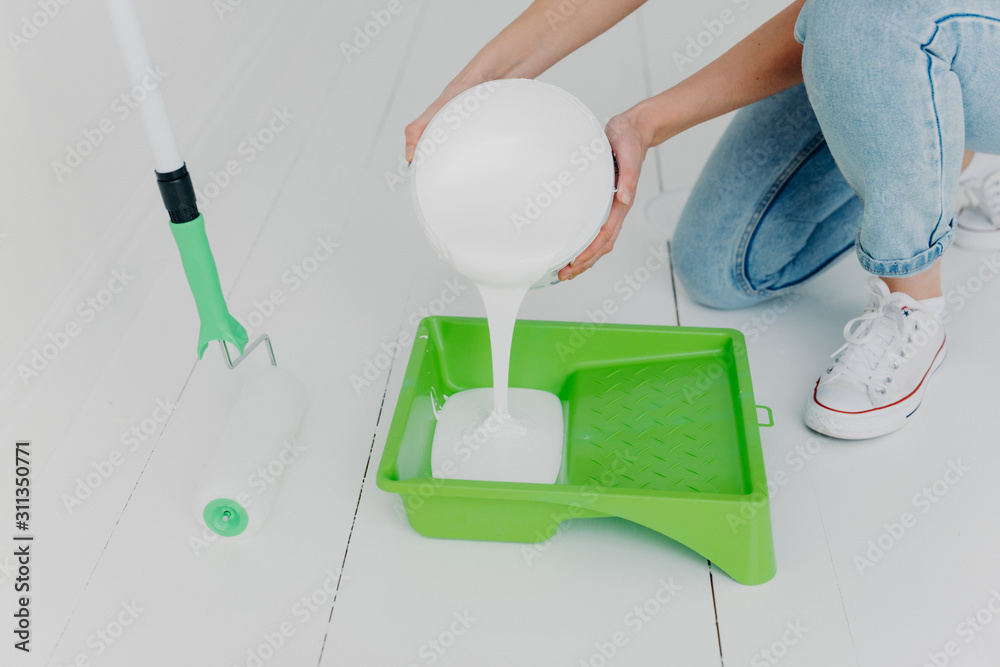 Cropped shot of unrecognizable woman pours white paint in tray, going ...