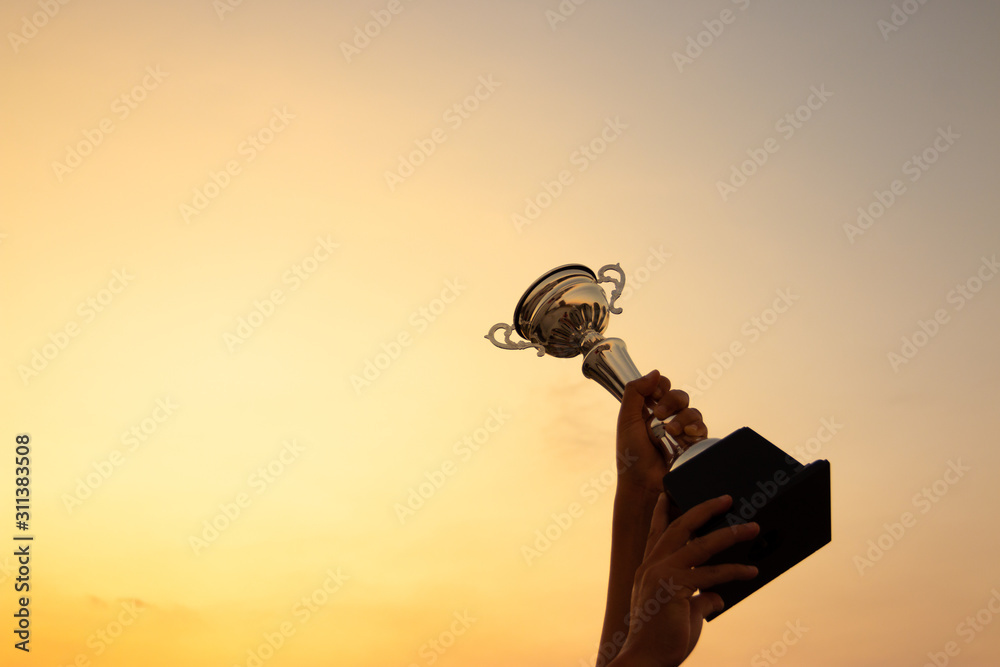 Victory concept with a hand holding a trophy on the sunset sky ...