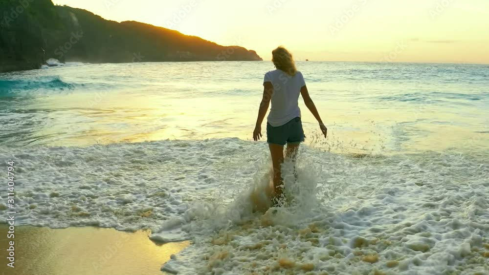 Back view of woman walking on ocean beach and bigger waves. Backside ...