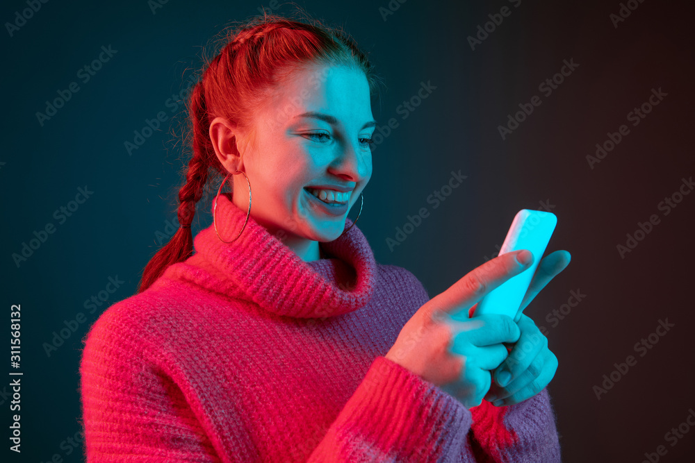 Using phone, smiling. Caucasian woman's portrait isolated on gradient ...