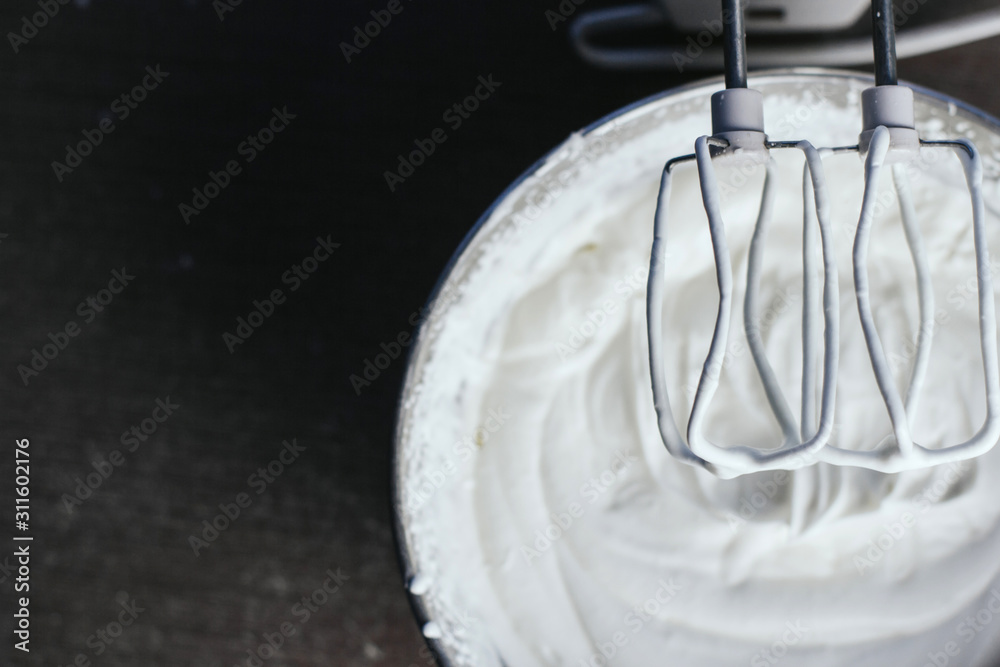 Beating a white cream with a mixer in a metal bowl. Whipped cream ...