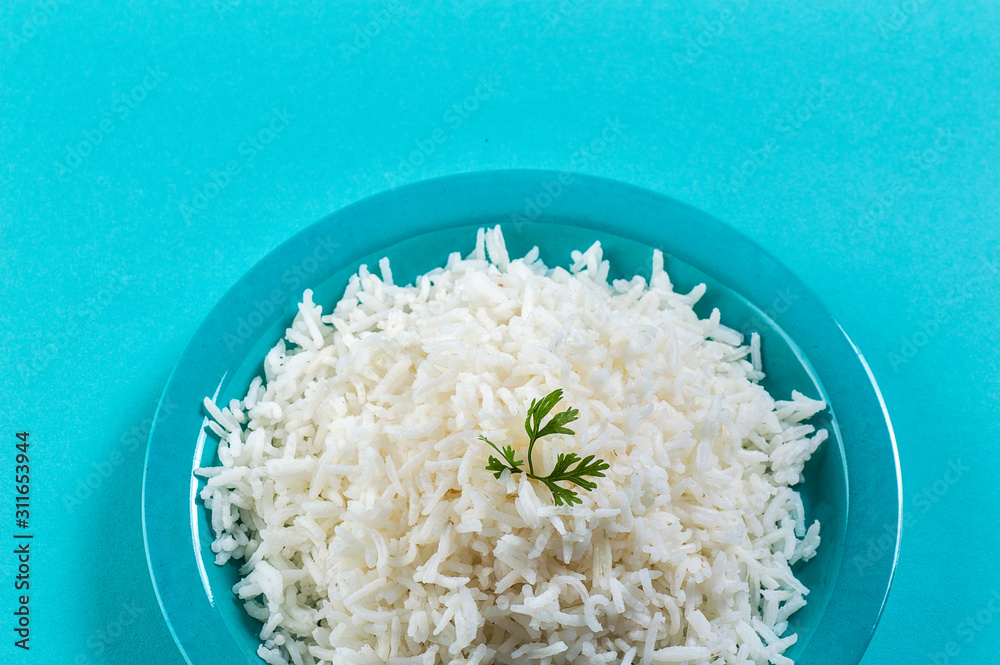 Cooked plain white basmati rice with corriander in a blue plate on blue ...