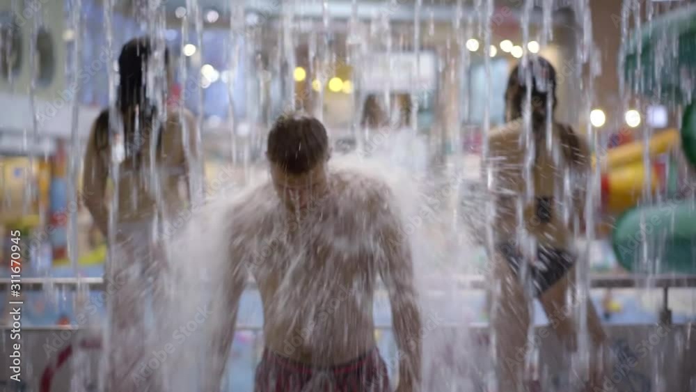 In the water Park behind the waterfall are two girls and a guy between ...