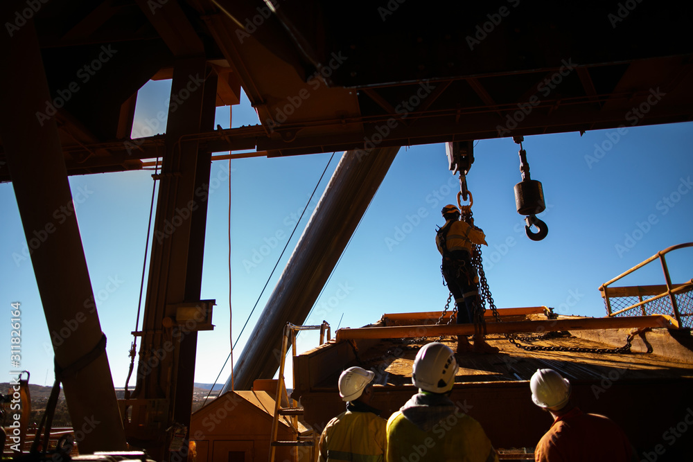 Rigger wearing safety hard hat working at height connecting chains into ...