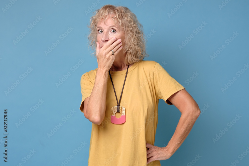 Scared senior woman looks at camera makes big eyes covering mouth with ...