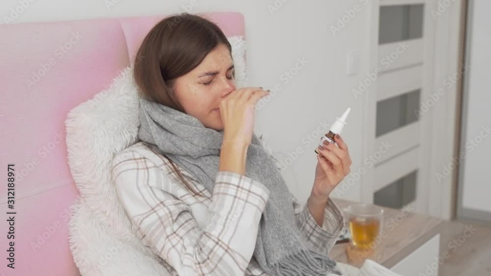 sick girl lying in bed coughing and sniffing, girl applies nasal spray ...